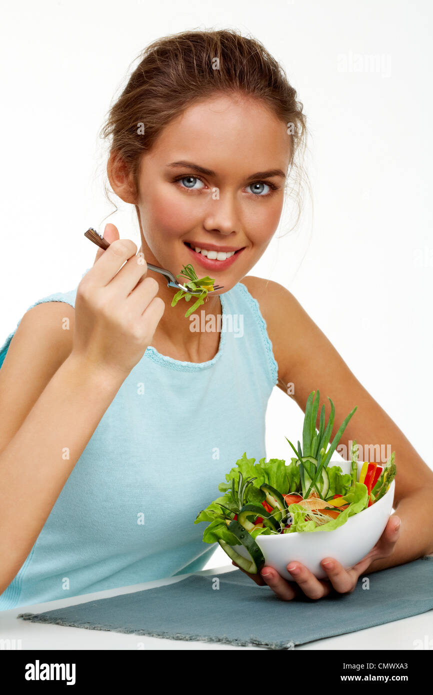 Portrait of pretty young girl with fork and bowl in hands eating ...