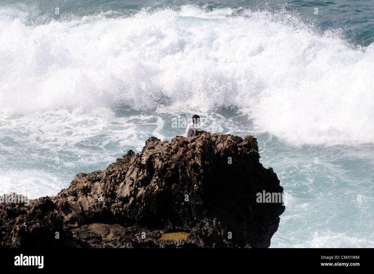 View of a brave man fishing off a large rock whilst the huge waves of ...