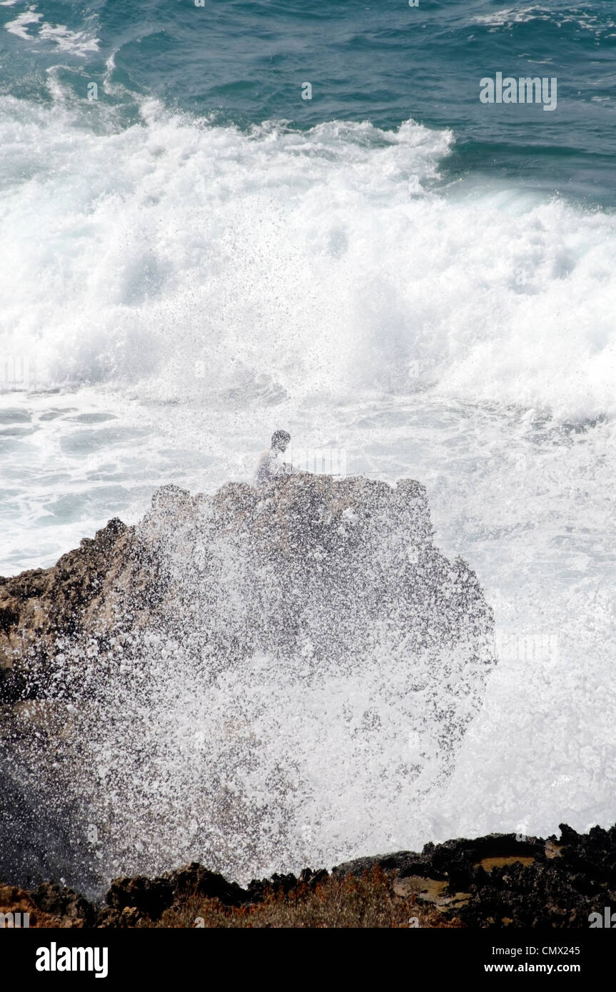 View of a brave man fishing off a large rock whilst the huge waves of ...