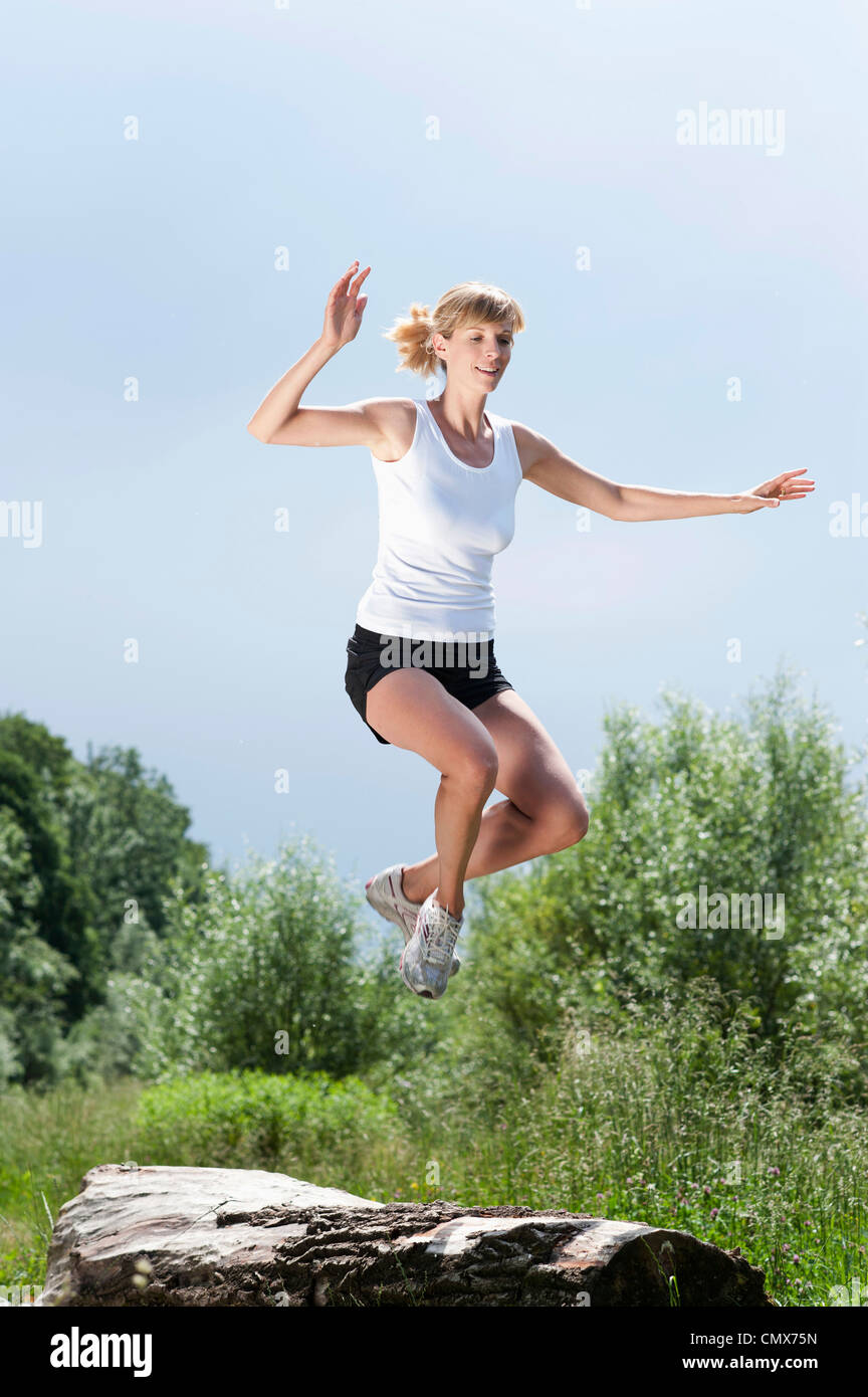 Germany, Bavaria, Mid adult woman jumping on tree stump, smiling Stock ...