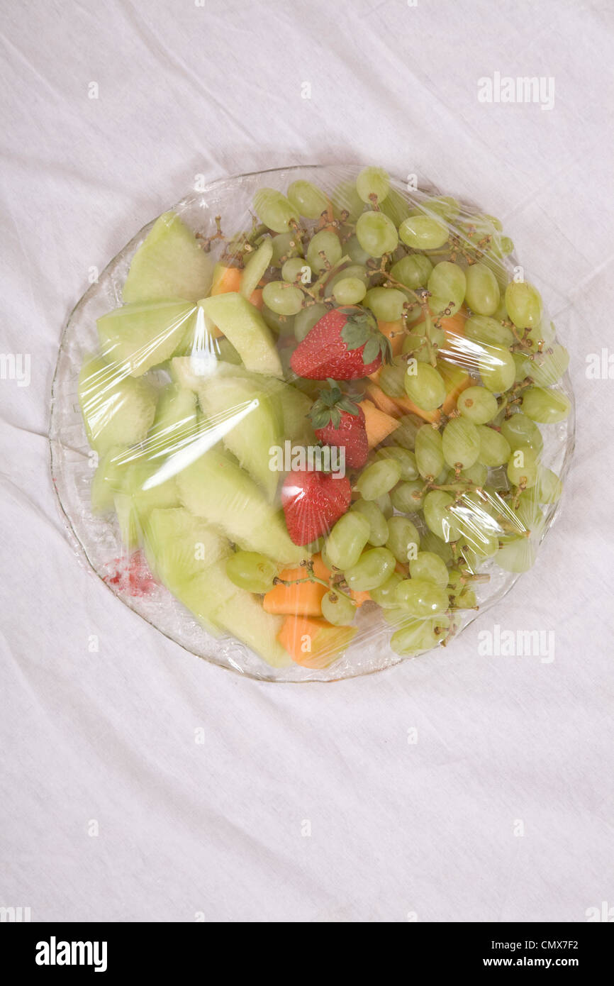 Plate of fruit with strawberries and white grapes covered in cling film ...