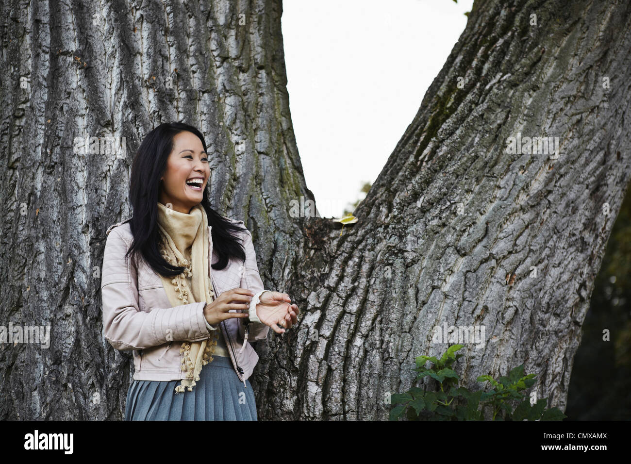 Germany, Cologne, Young woman near tree trunk in park, smiling Stock ...