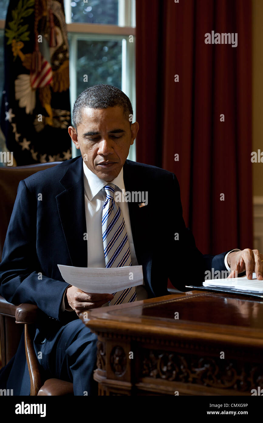 President Barack Obama reads a document at his desk in the Oval Office ...