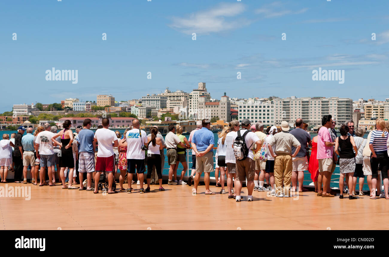 Passengers crowd the bow of a cruise ship as it approaches the port of ...