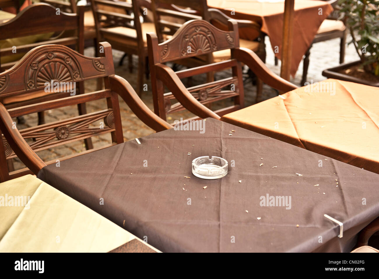 An ashtray in the center of a dirty, brown cafe table. Tan tables ...