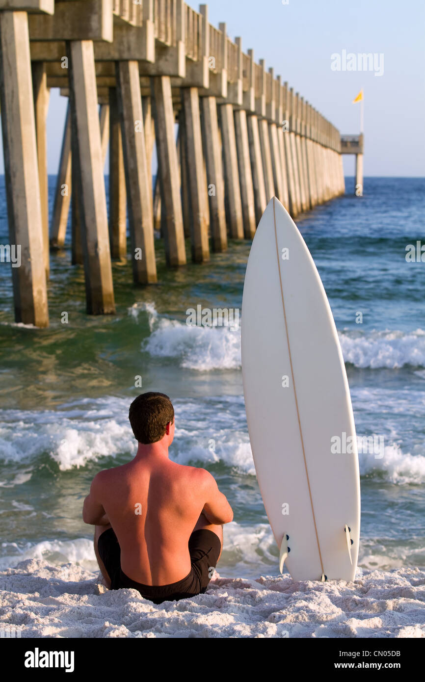 Surfer sits watching the waves in the sand at the beach next to his ...