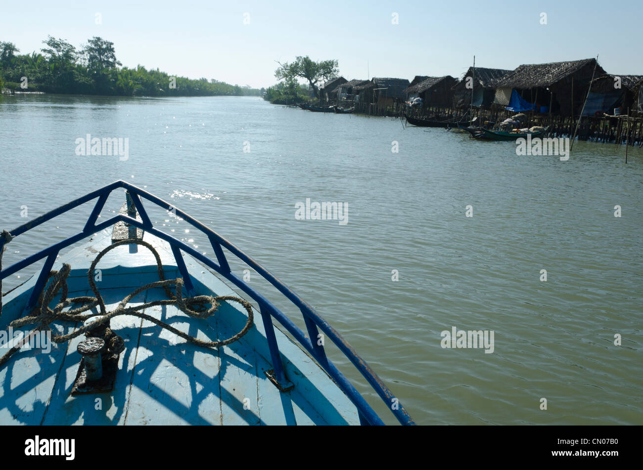 Boat navigating along a waterway with bamboo huts in the Irrawaddy ...