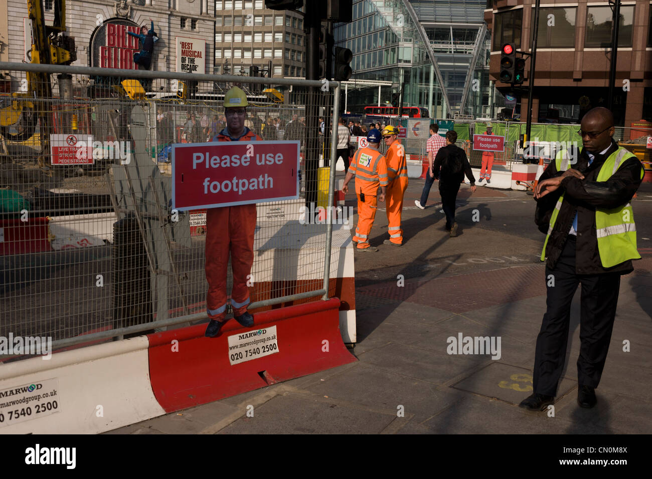 Man checks his watch near a scaled human workman figure who warns ...