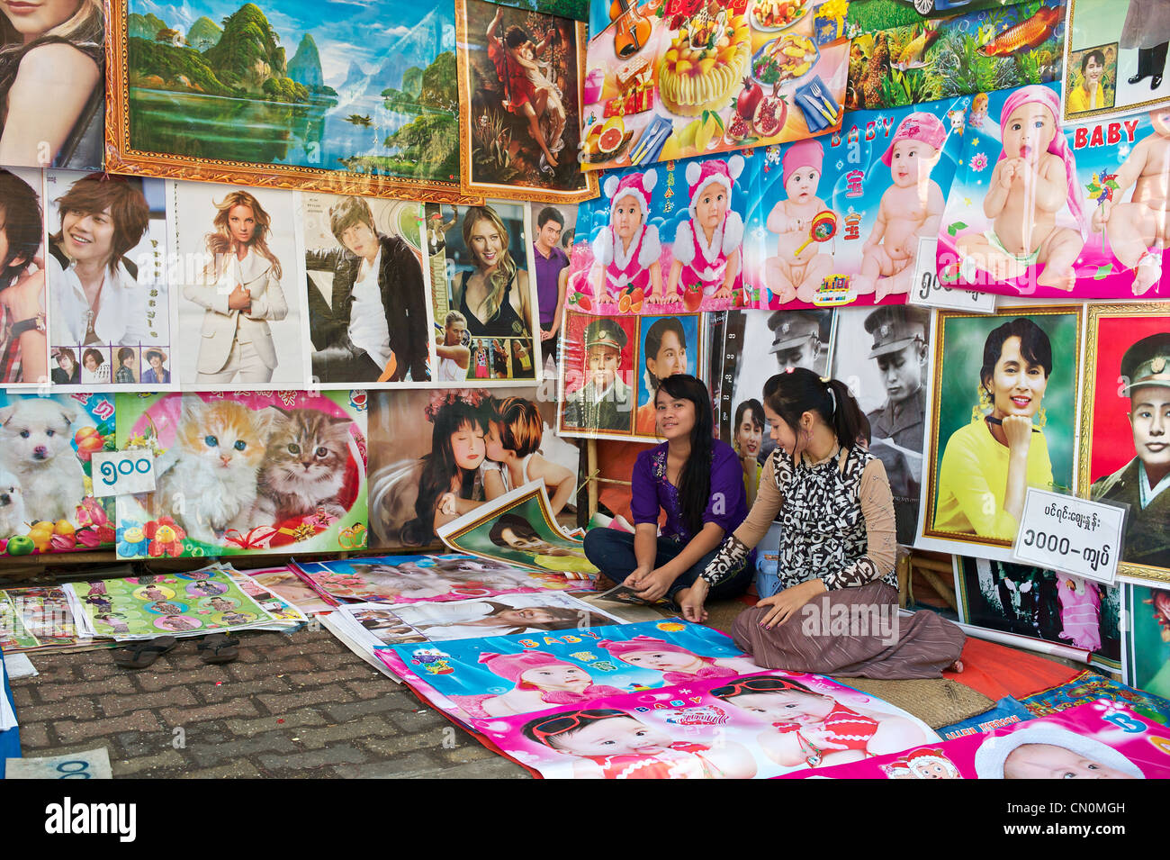 Two young Burmese girls sell colourful posters at a street stall ...