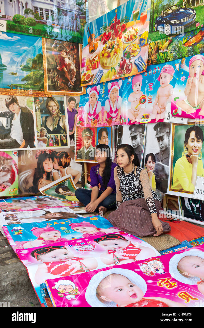 Two young Burmese girls sell colourful posters at a street stall ...