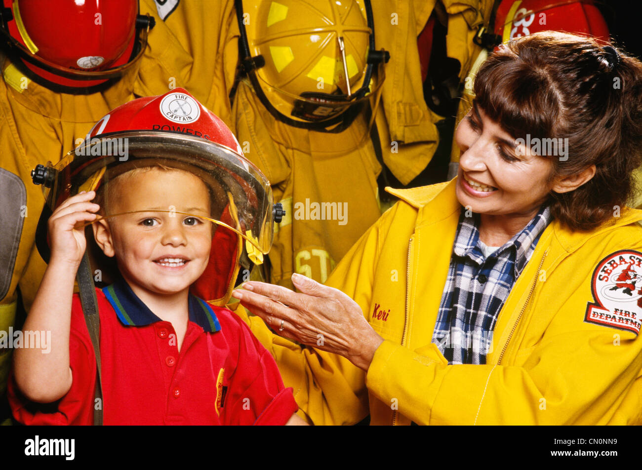 Female fighter fighter helps visiting small boy with fire helmet Stock ...