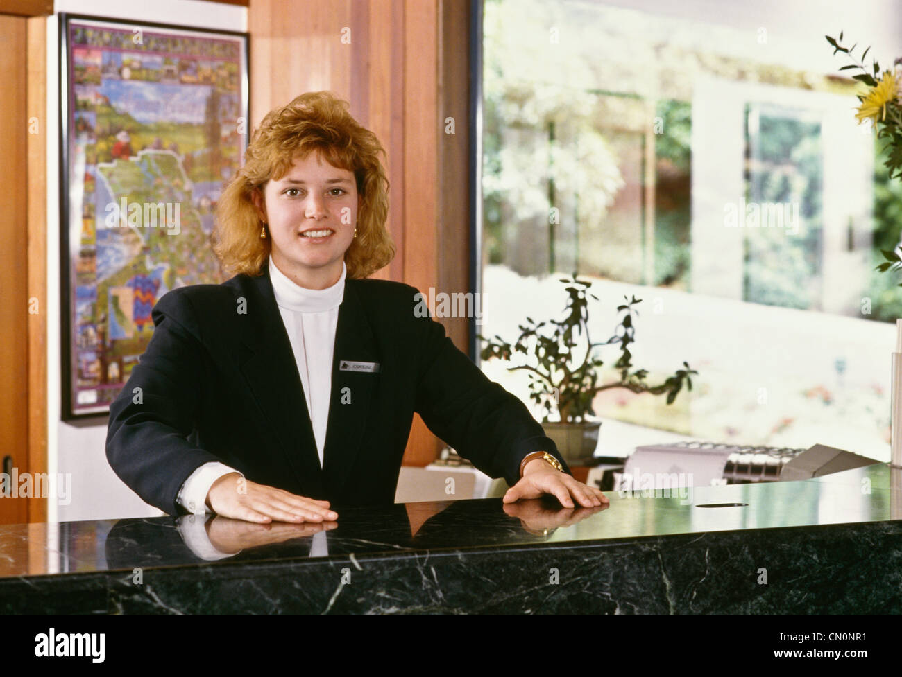 Smiling young woman employee mans the front reception desk at hotel ...