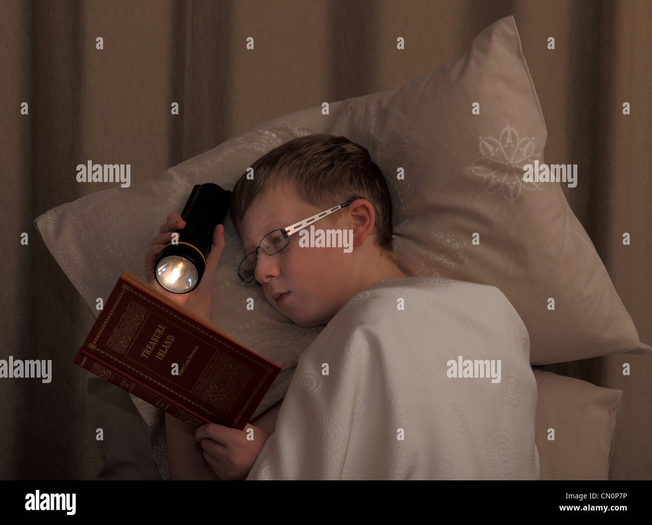 A 12 year old boy reading a book, (Treasure Island), in bed by ...