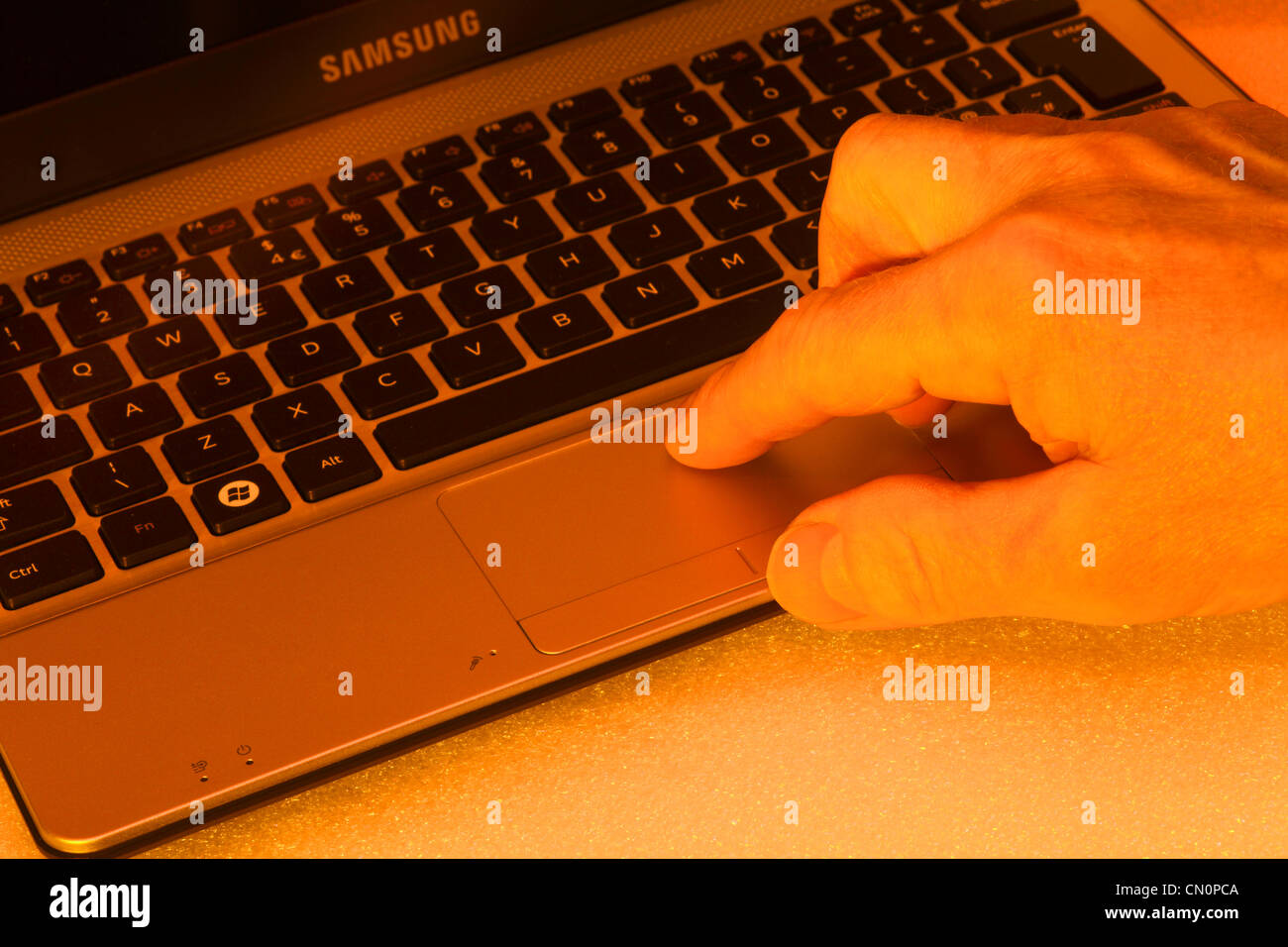 A mans hand using a netbook/laptop.Picture has an orange cast Stock ...