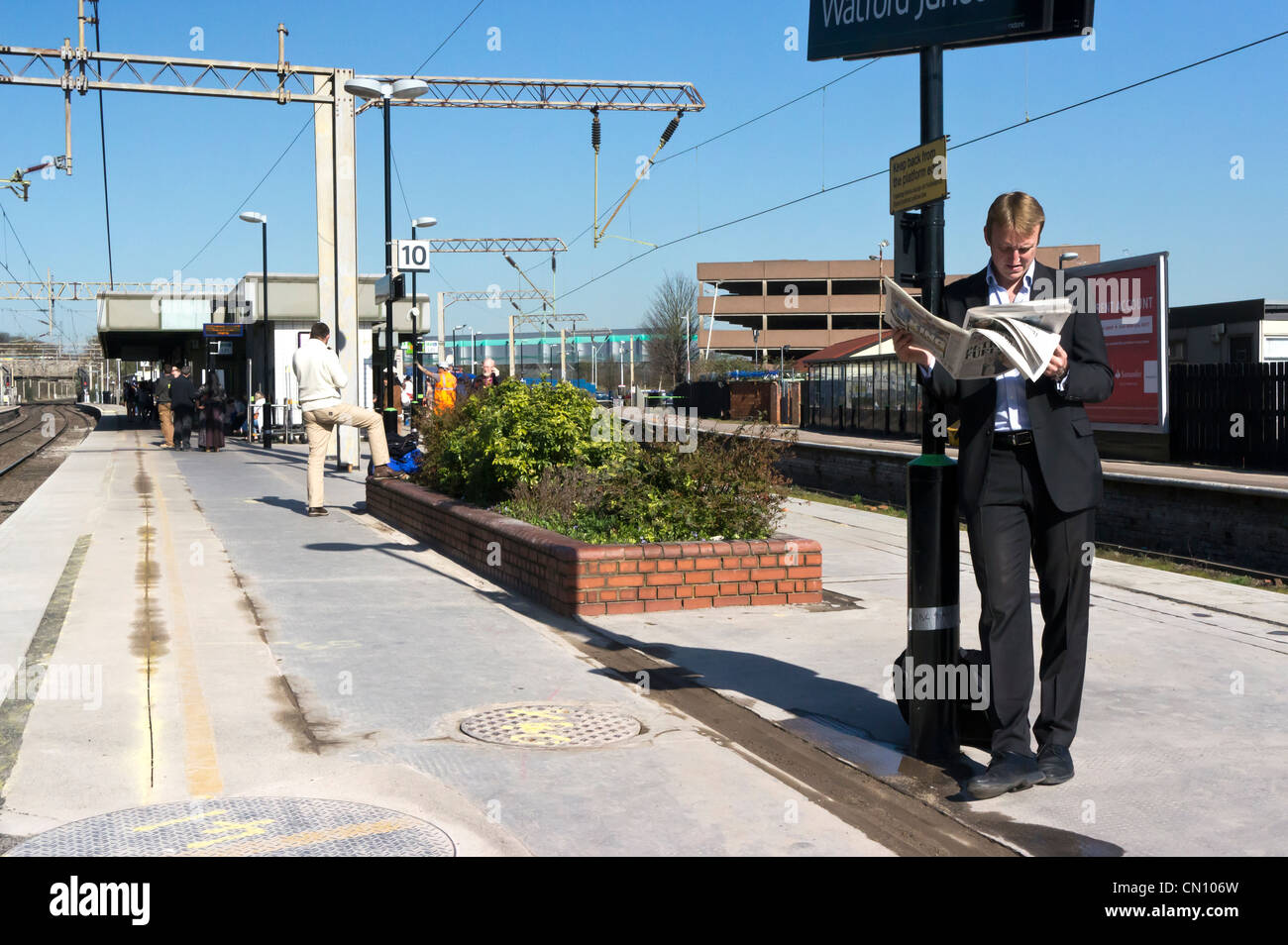 Man reading newspaper waiting for a train at Watford Junction railway ...