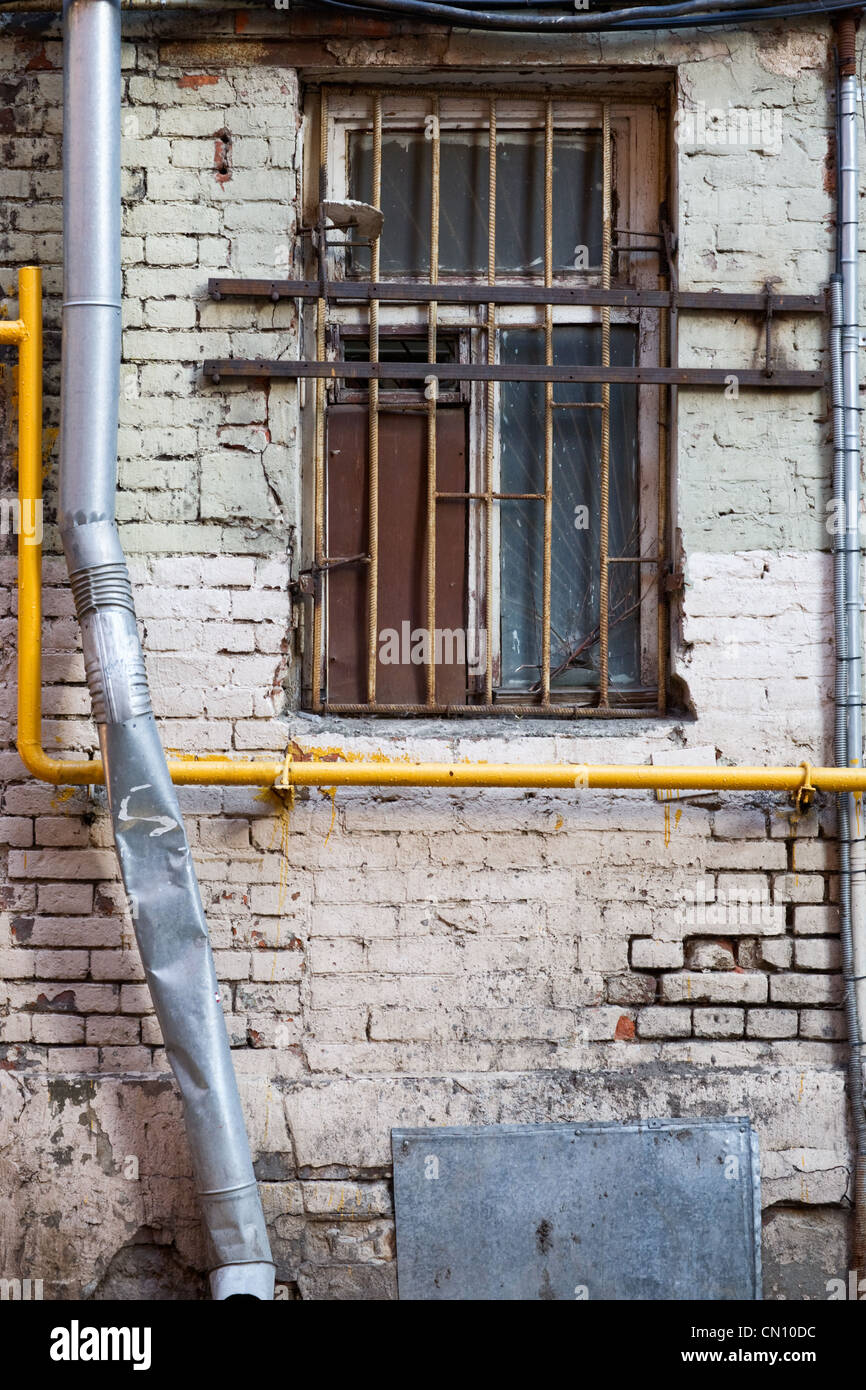 Latticed window, cables and water pipe on run-down brick wall Stock ...