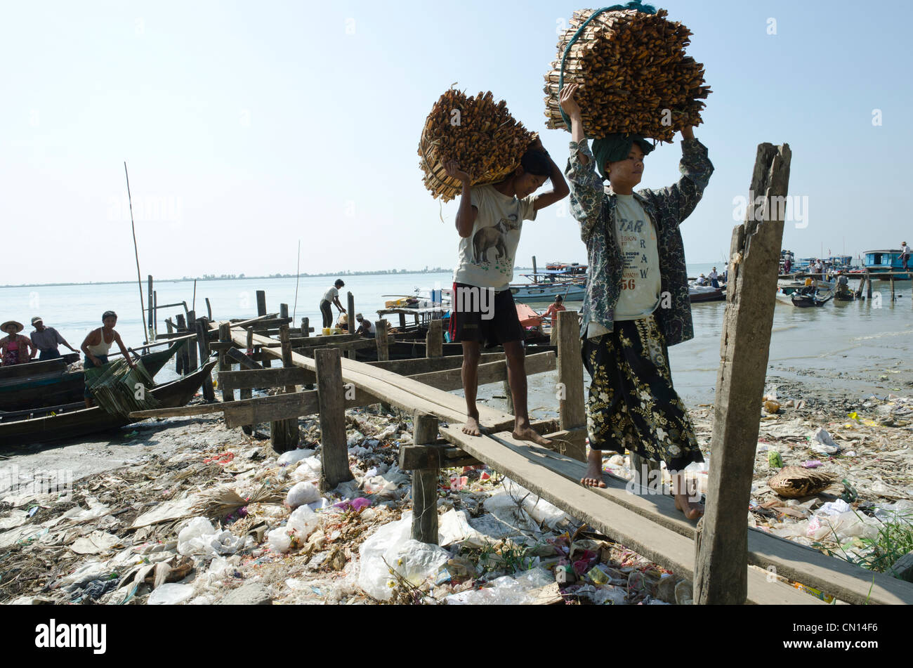 Two women carrying fire wood on a wooden jetty. Labutta harbour ...