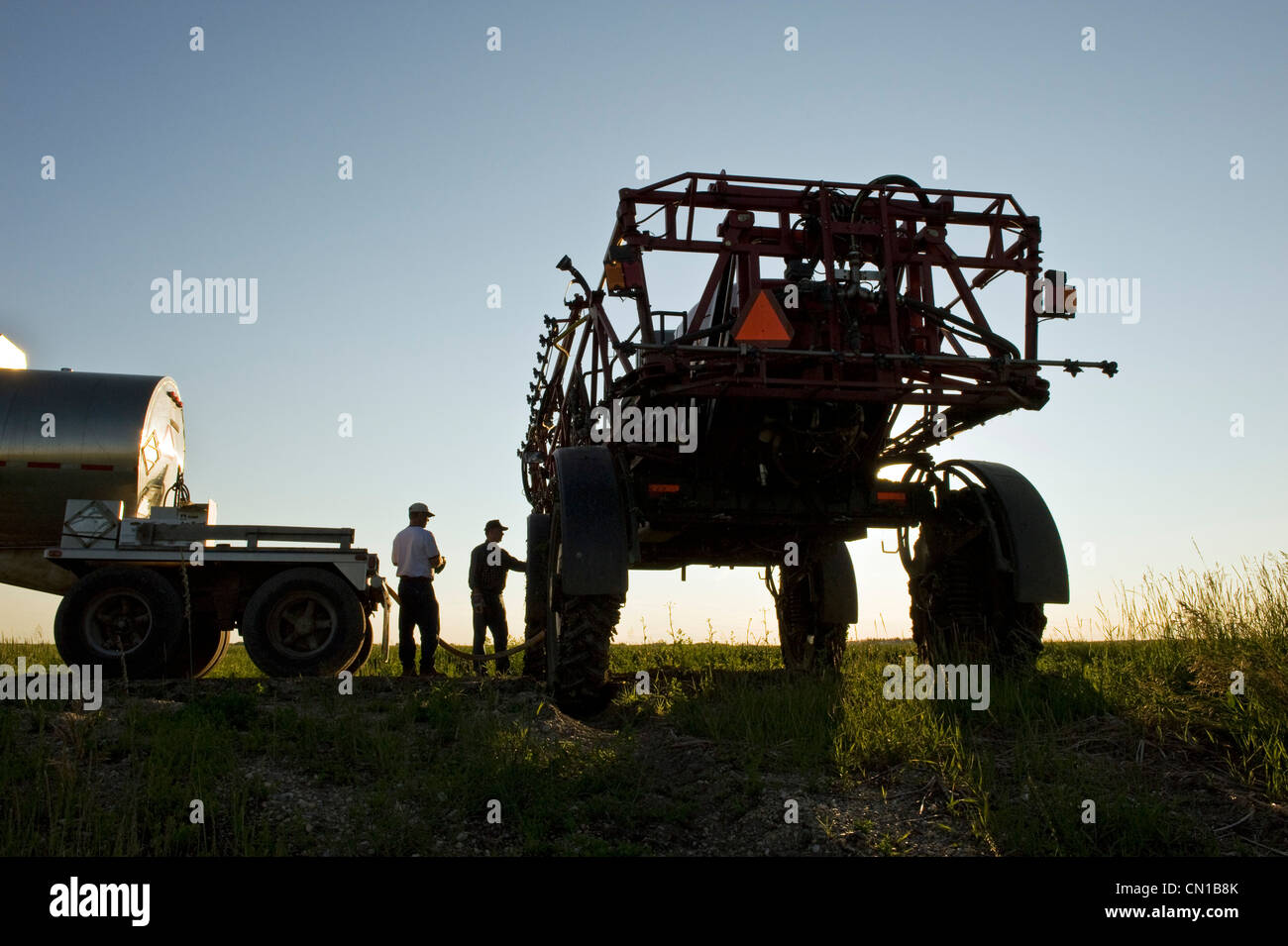 Two farmers load a high clearance sprayer with chemical fungicide and ...
