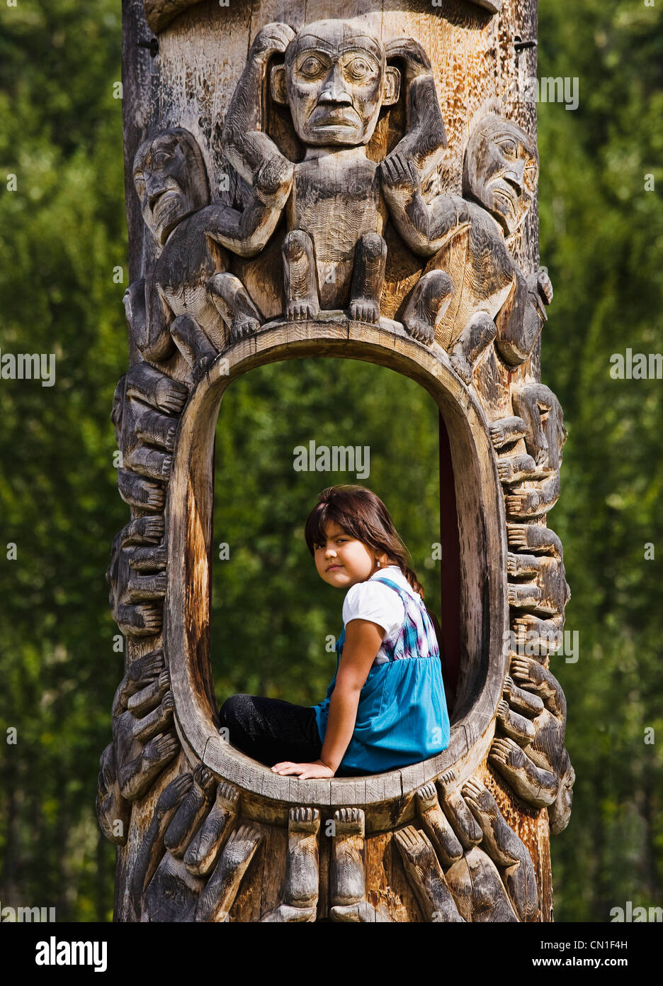 Young girl sitting in a totem pole, Kitwanga, Northern British Columbia ...