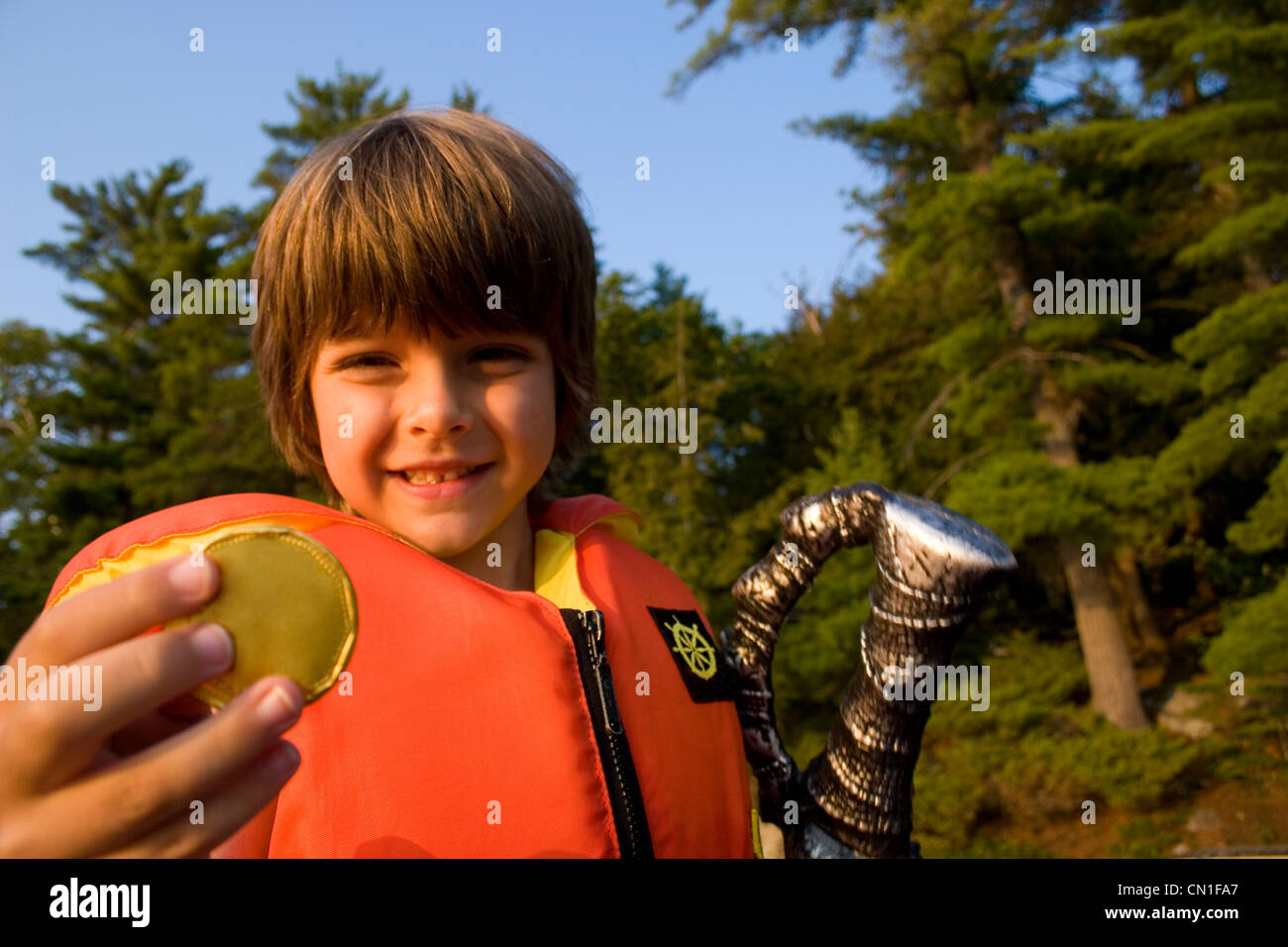 Portrait of a young boy in a life jacket holding a pirate sword and a ...