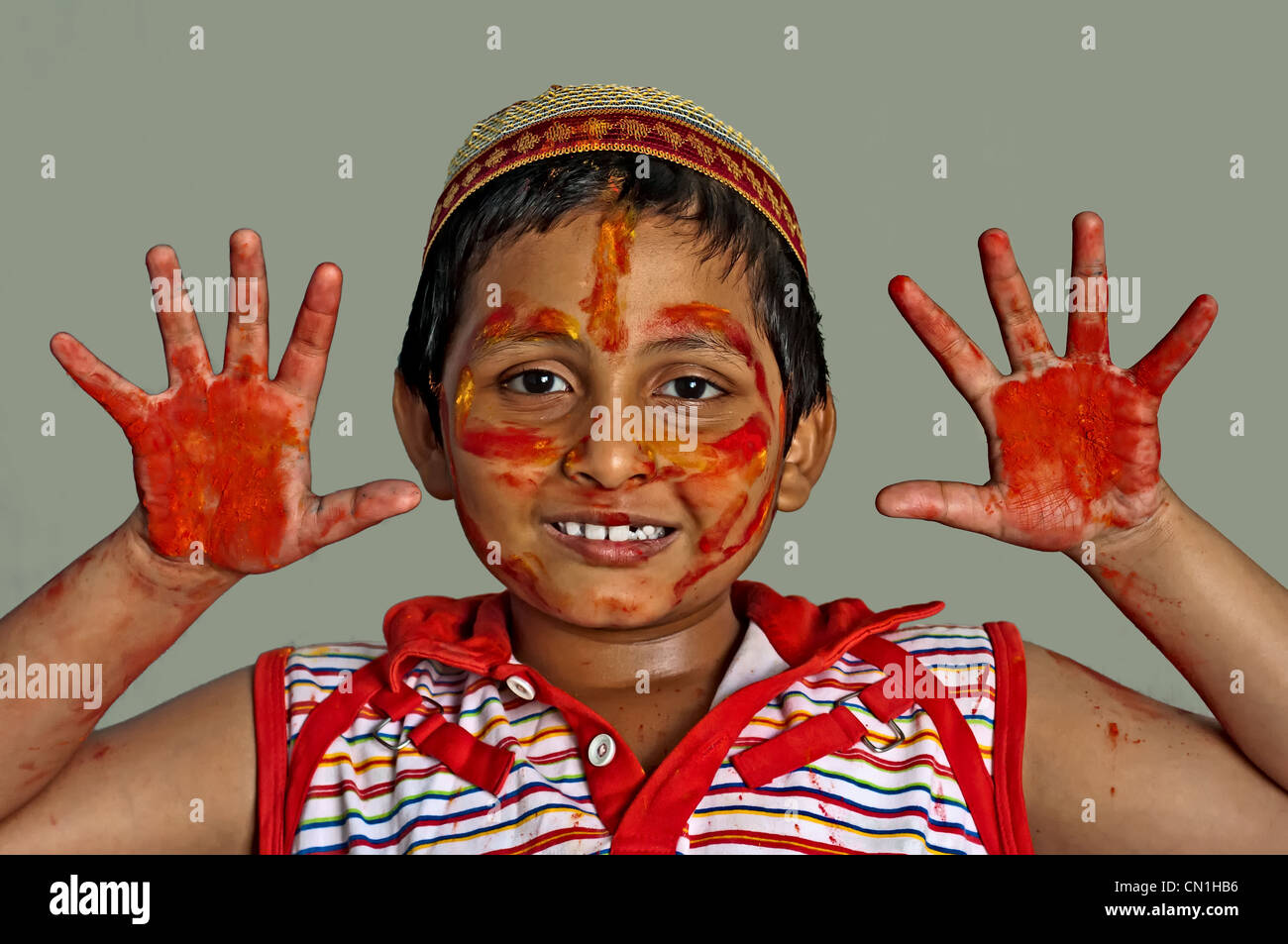 Young boy playing Holi, smiling with colors on face and hands, with cap ...