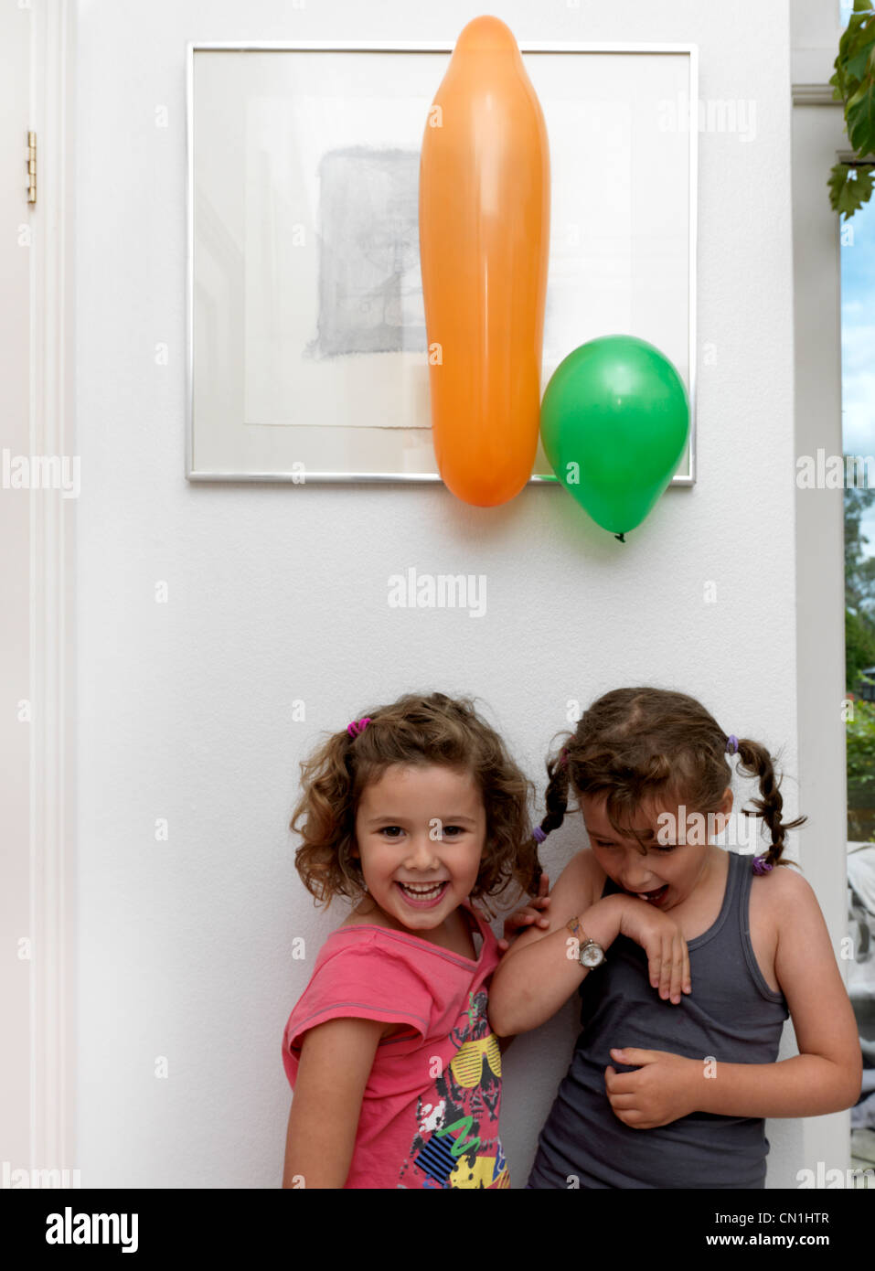 Young Girl Nudging Sister With Her Elbow Standing Under Balloons ...