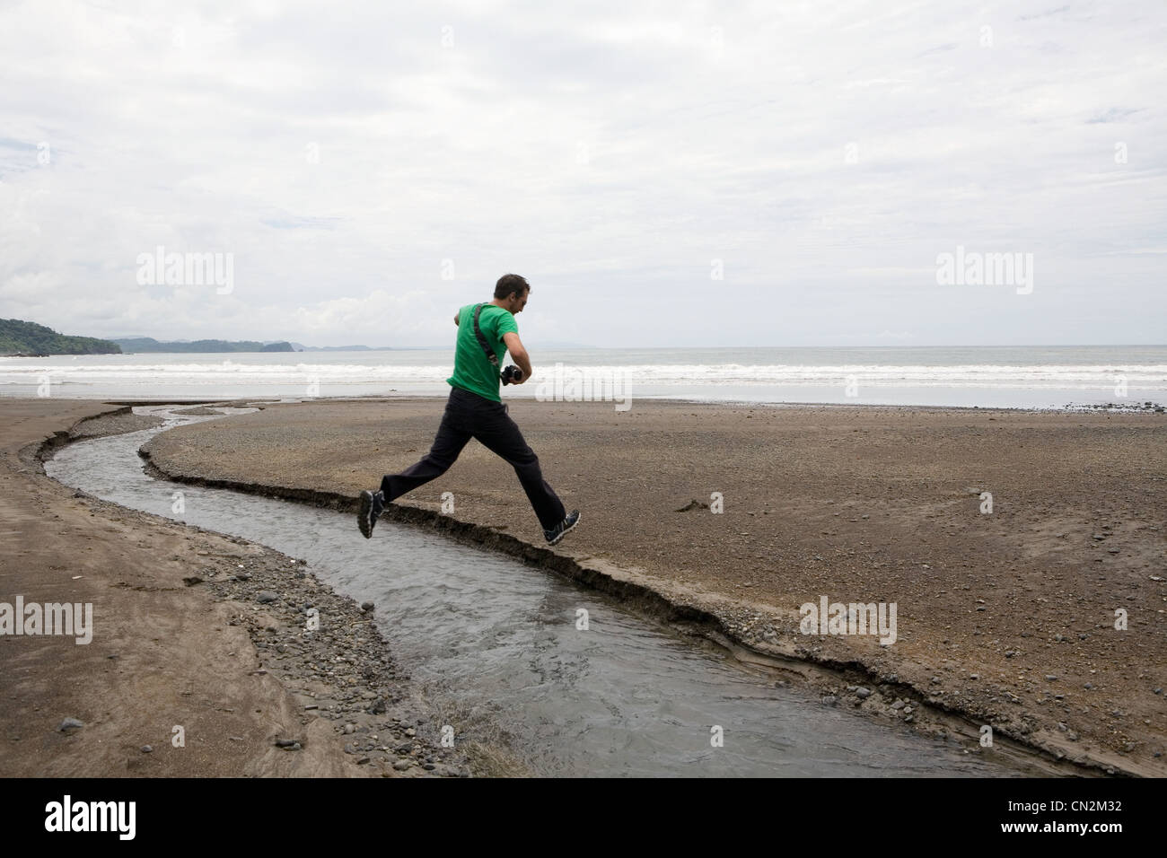 Man jumping over stream on beach Stock Photo - Alamy