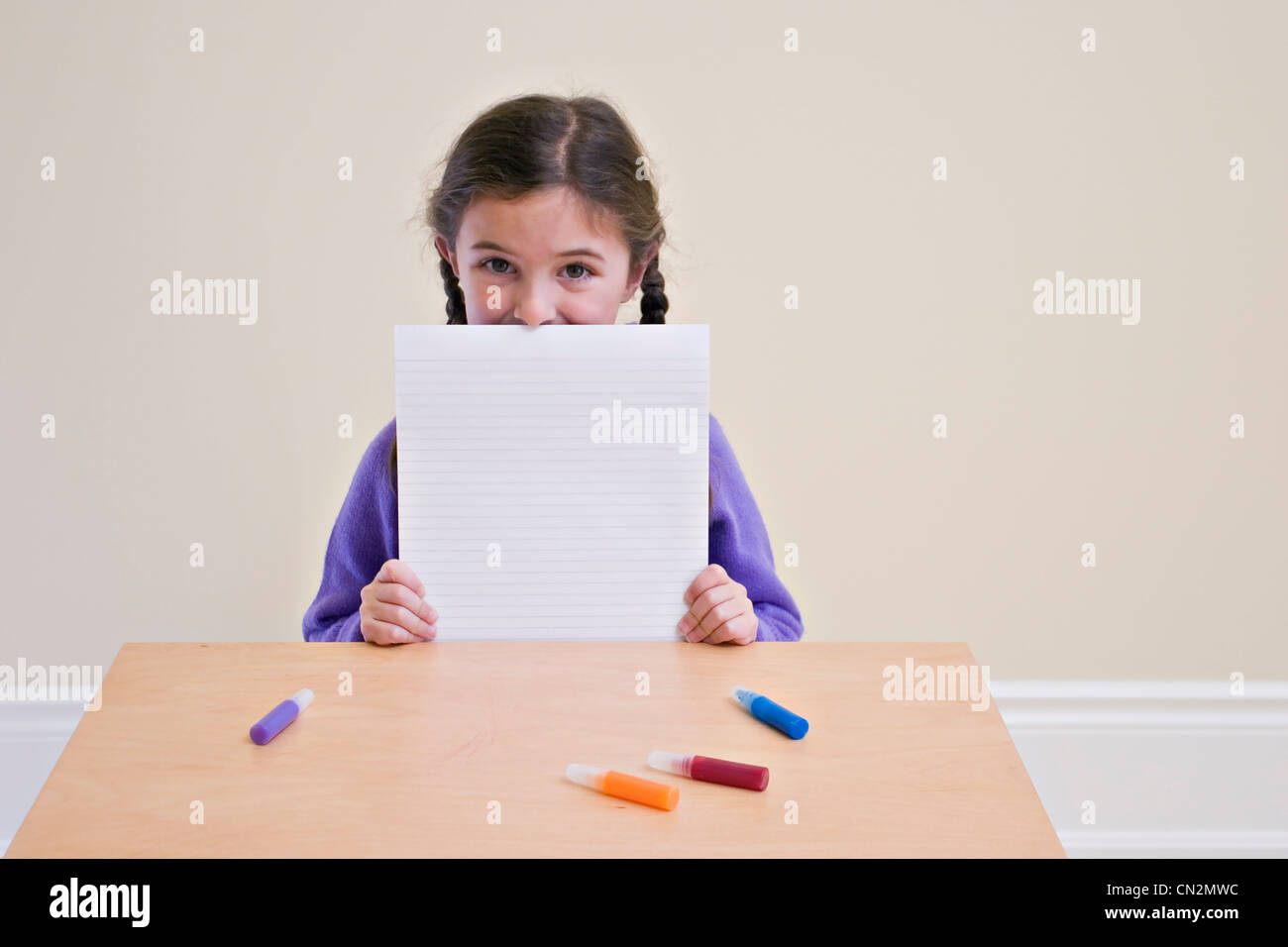 Young Girl Sitting at Desk Holding up Pad of Paper Stock Photo - Alamy