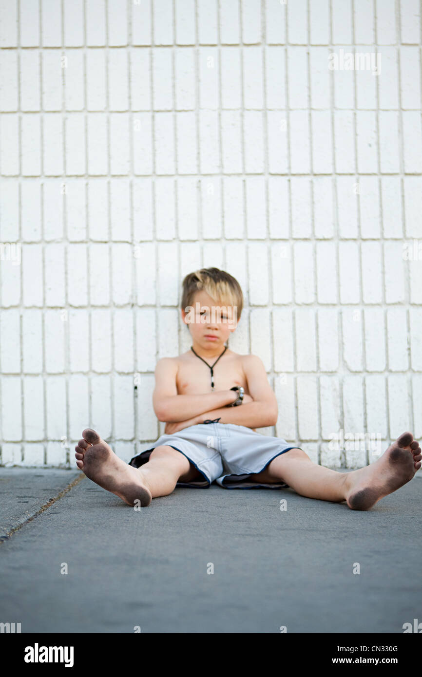 Boy with dirty feet sitting by brick wall Stock Photo - Alamy