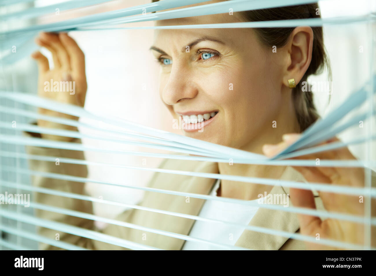 Smiling business woman looking out of the window with blinds Stock ...