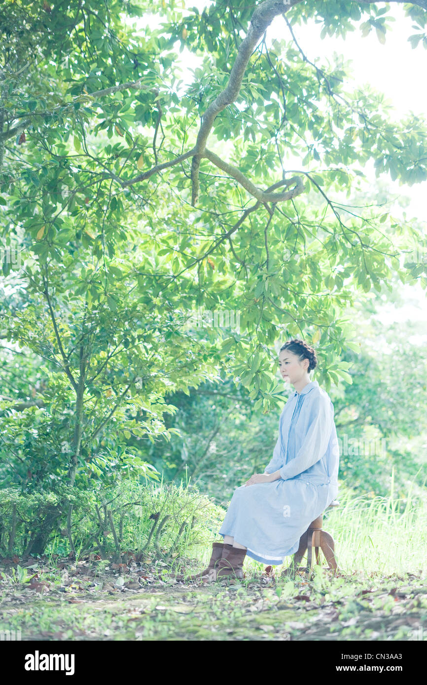 Young woman sitting on stool by trees Stock Photo - Alamy