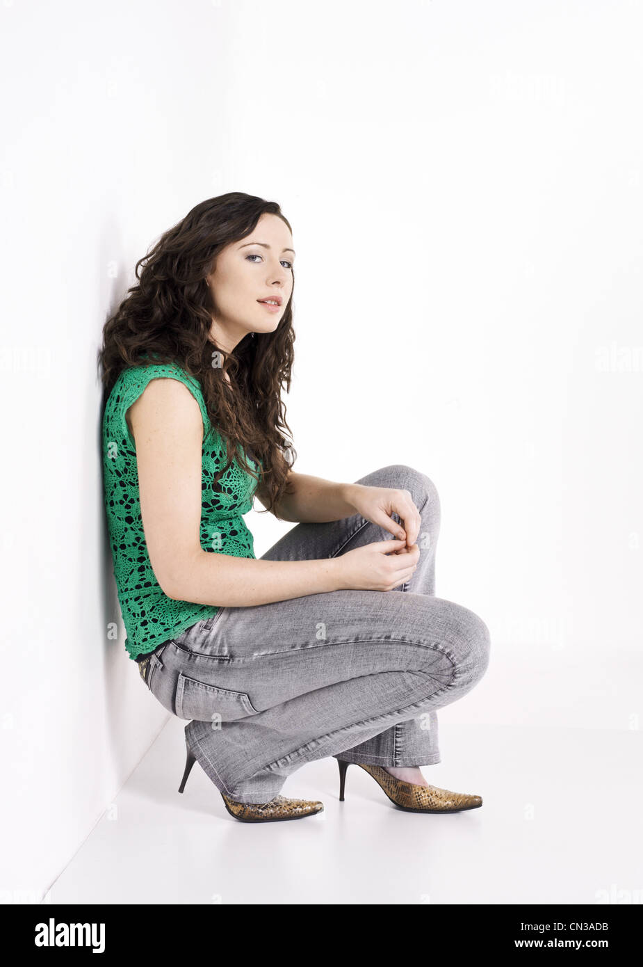 Woman crouching against white wall, portrait Stock Photo - Alamy