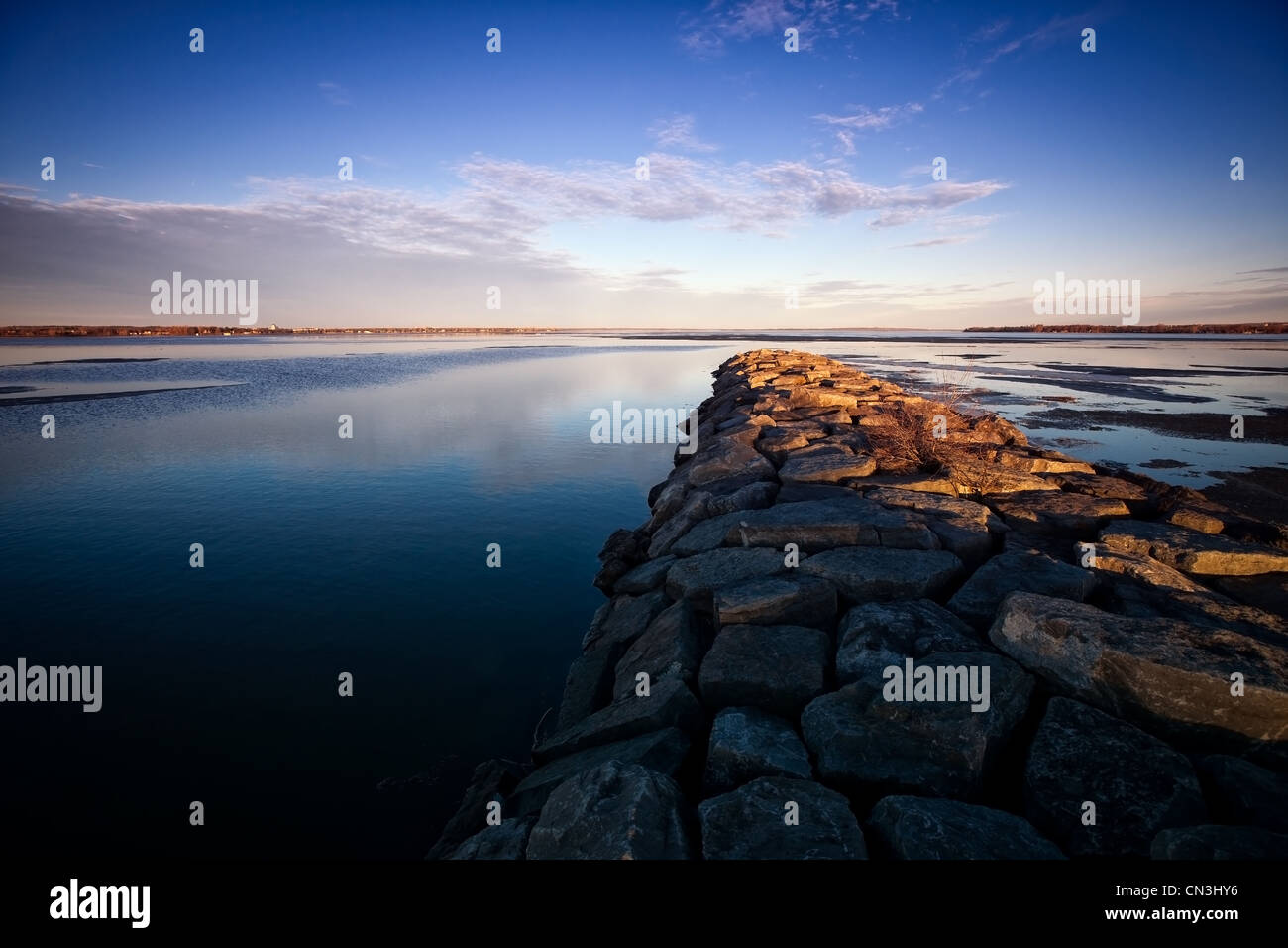 A stone jetty reaches toward the horizon on the calm waters of the ...