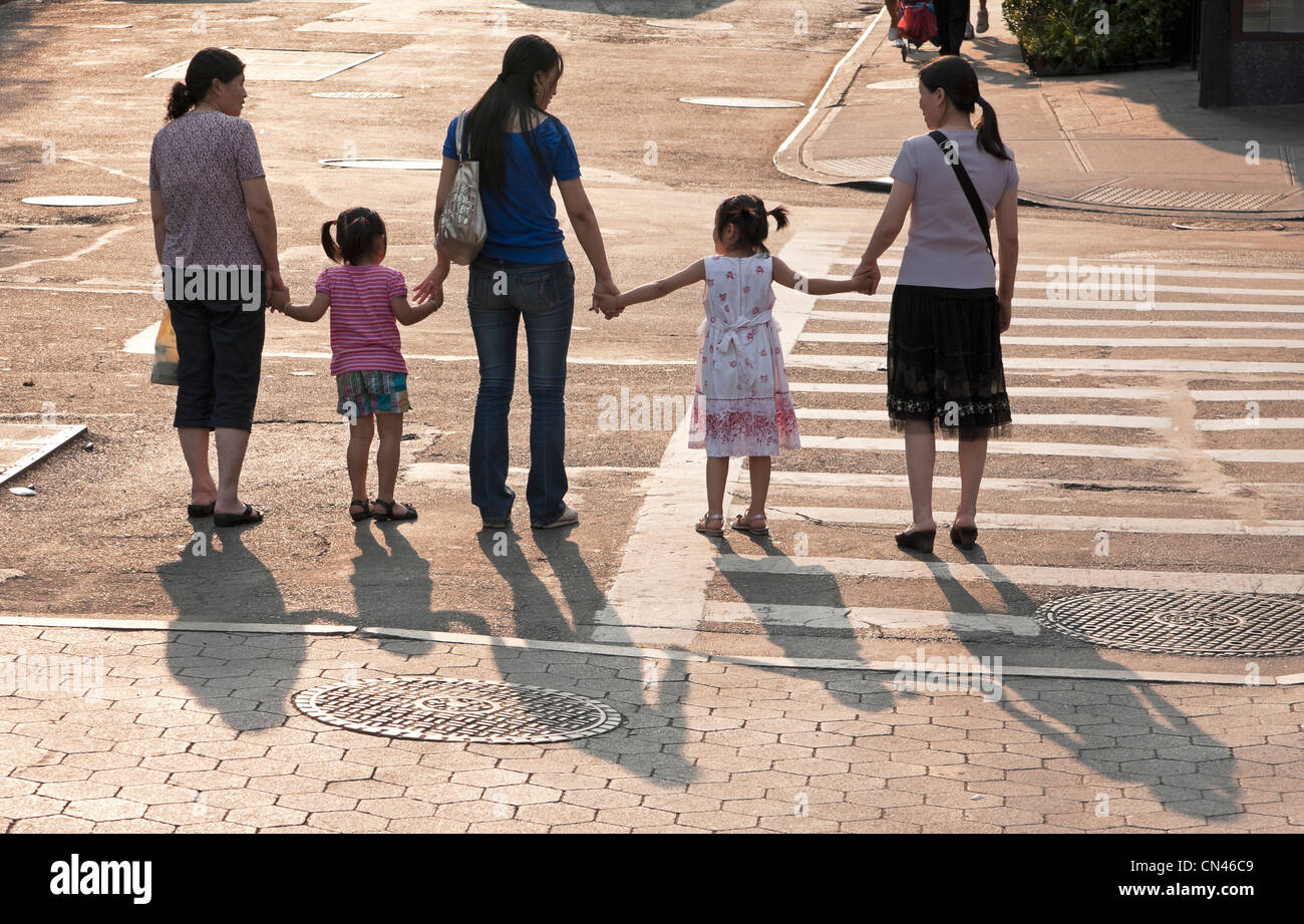 Adults and children hold hands as they cross a street in Chinatown in ...
