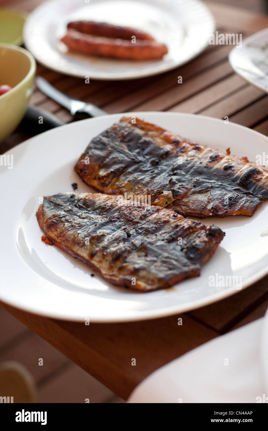 Grilled mackerel fillets on a white plate with a blurred background of ...
