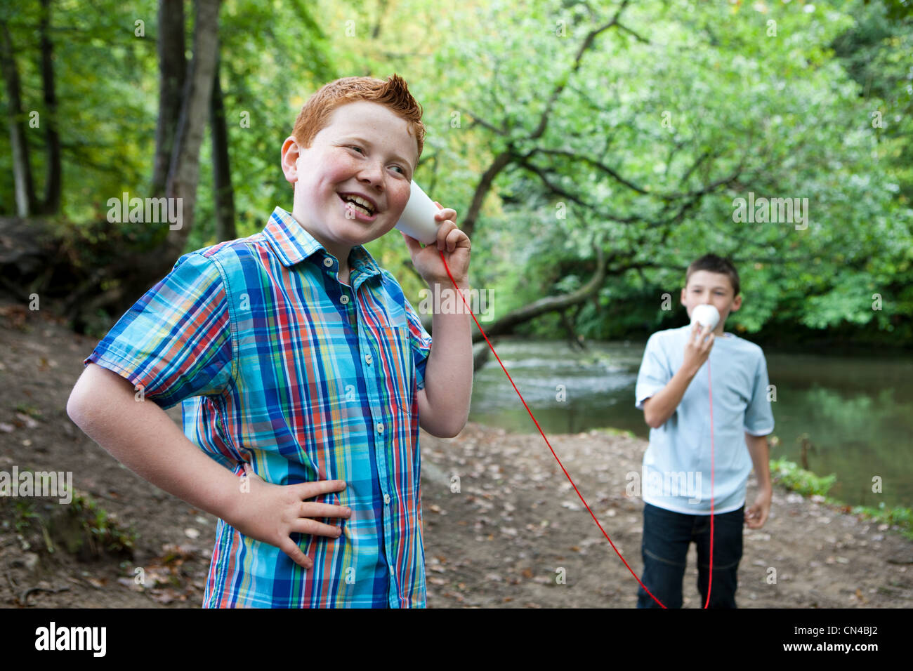 Two boys using paper cups and string to communicate in woodland Stock ...