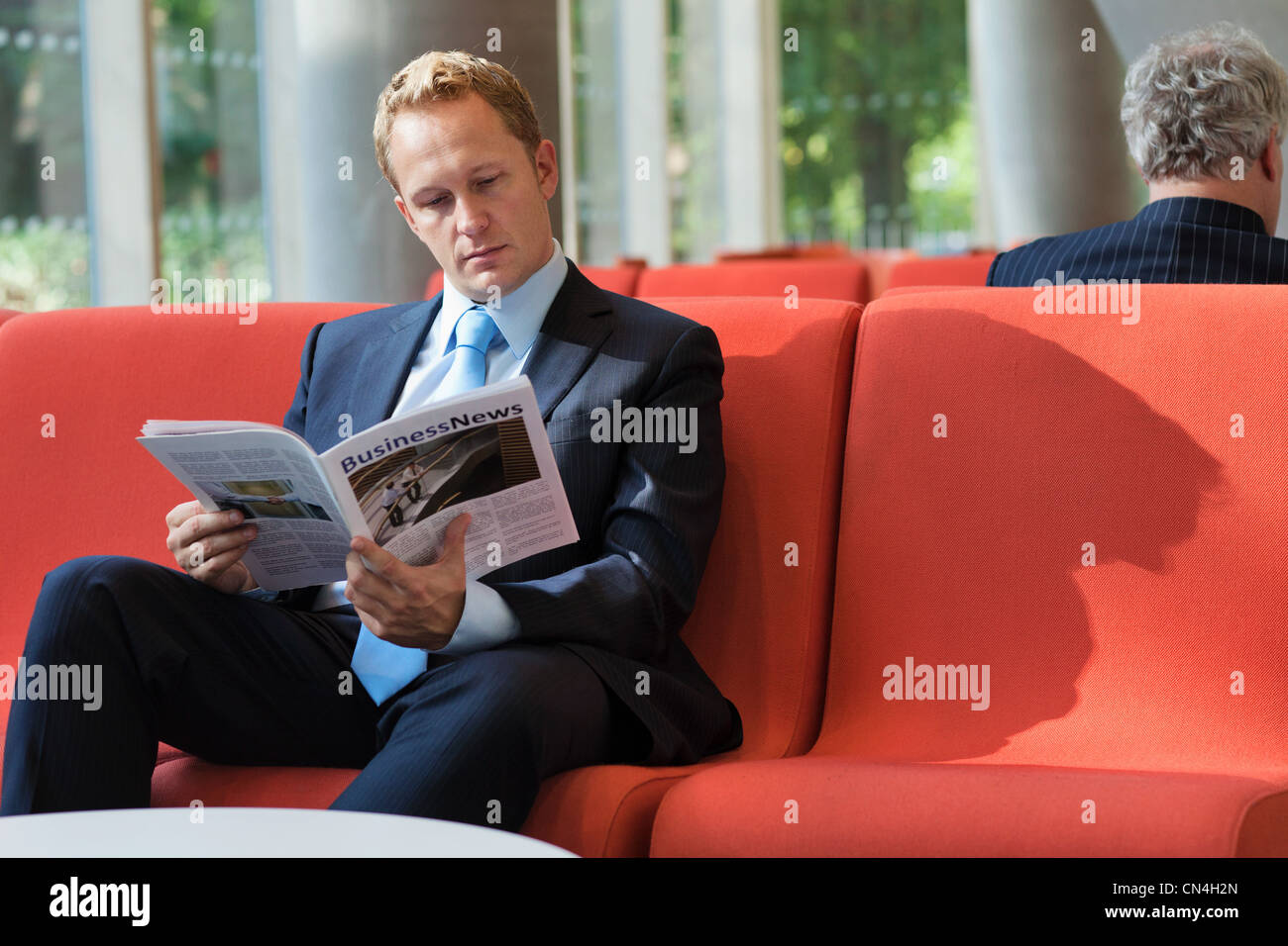 Businessman reading magazine in office lobby Stock Photo - Alamy