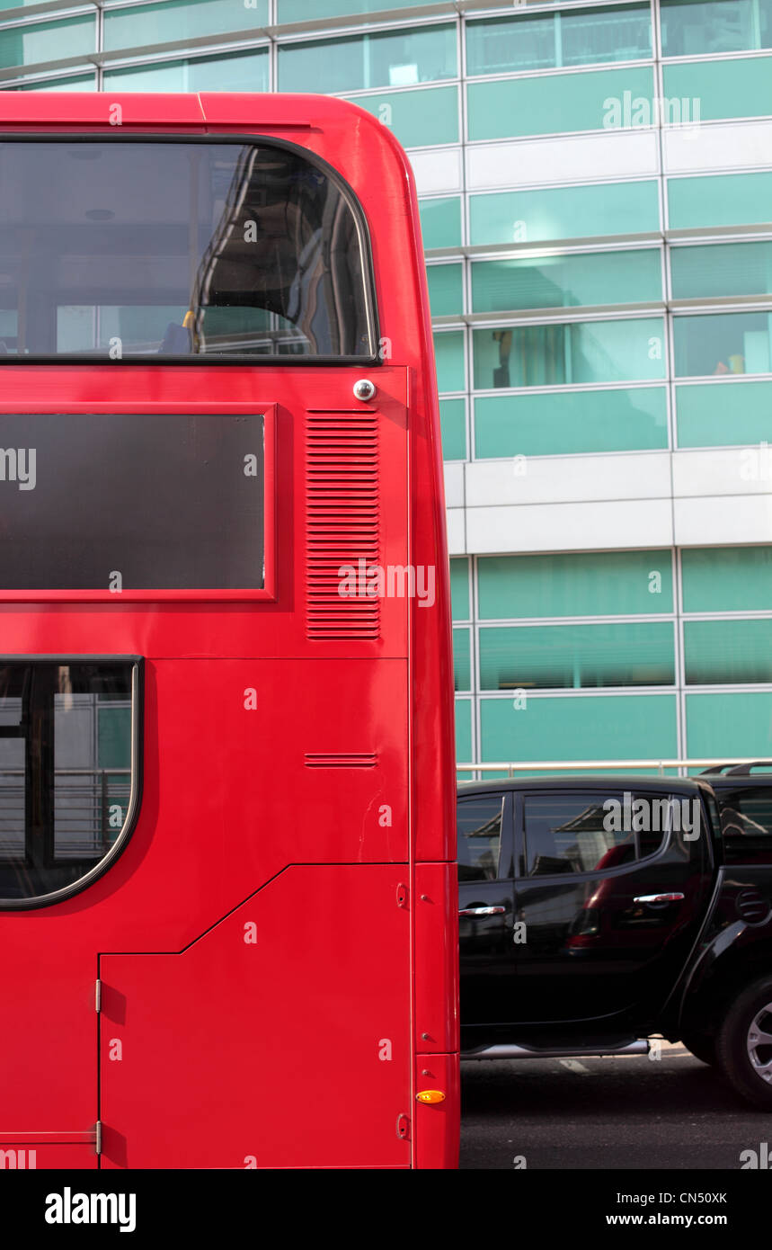 A red double decker bus passes a black car outside a green glass ...