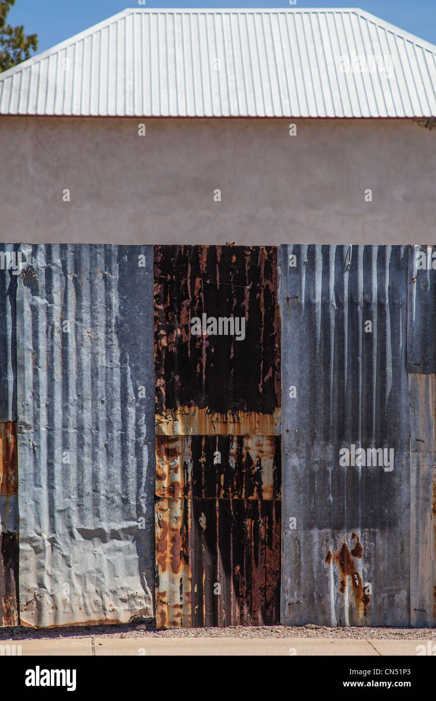 A tall corrugated metal rusted wall in front of a small white stucco ...