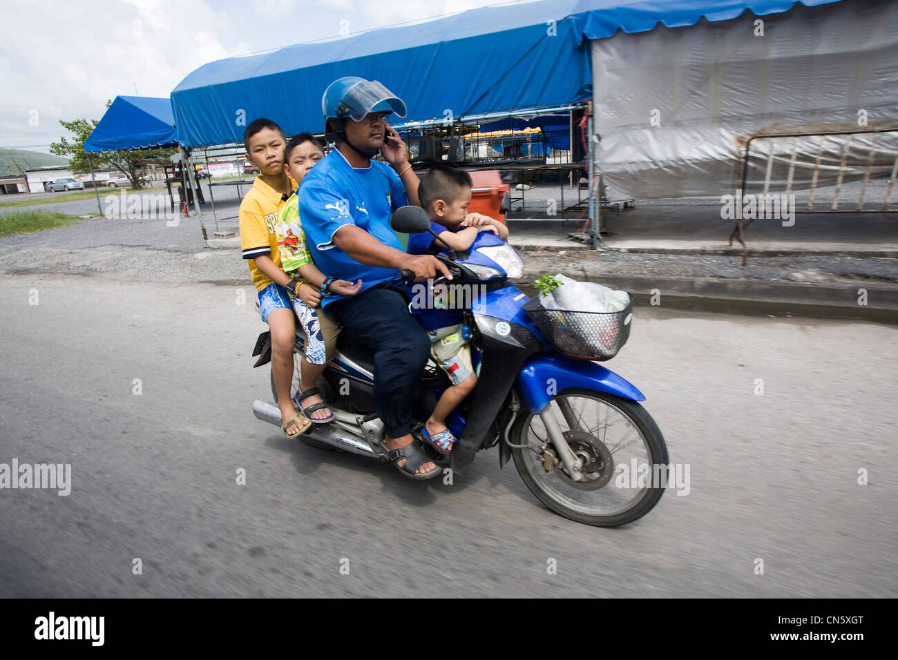 A father drives his motorcycle one-handed as he talks on his mobile ...