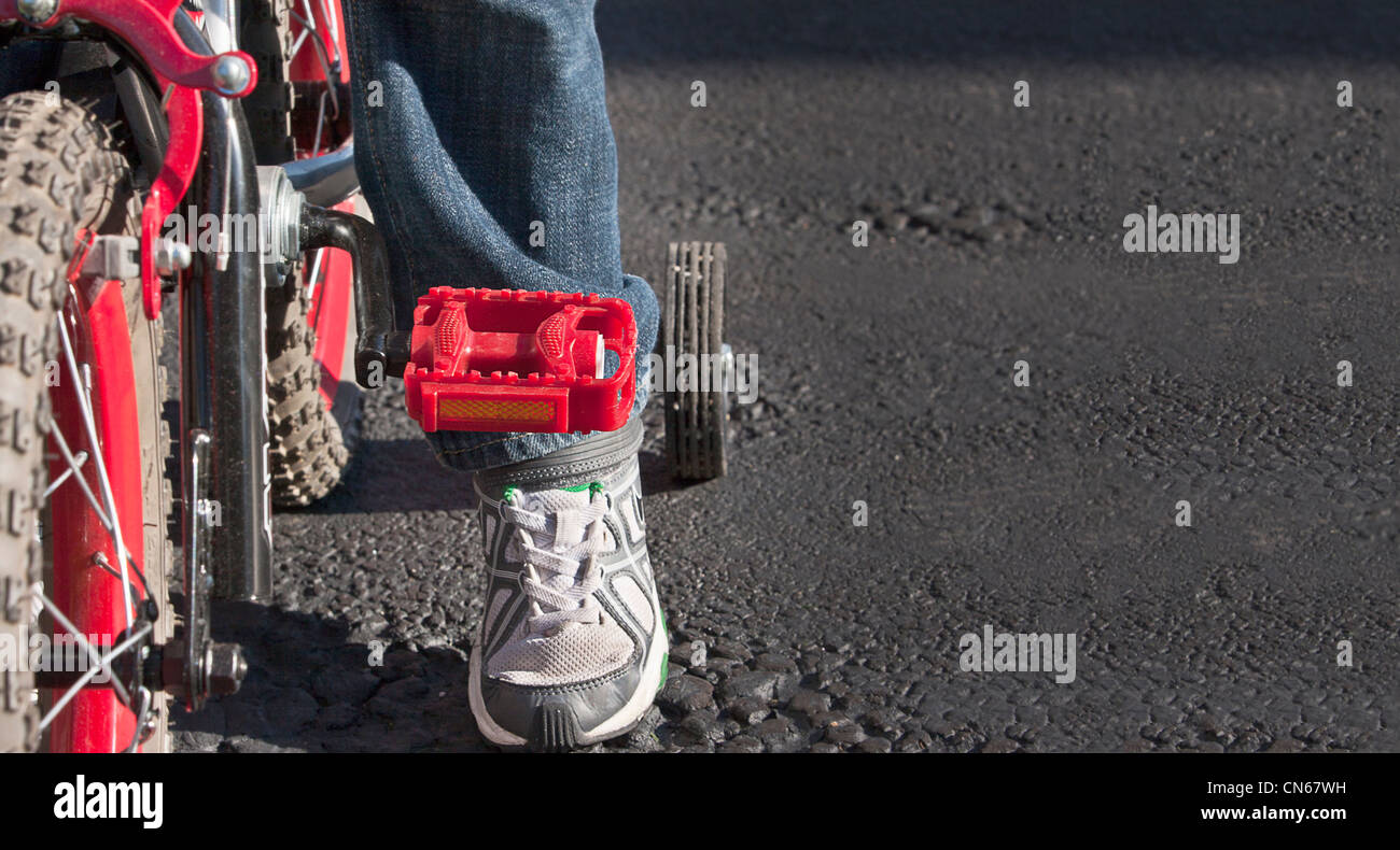 A child learns to ride a bike with training wheels, close crop of pedal ...