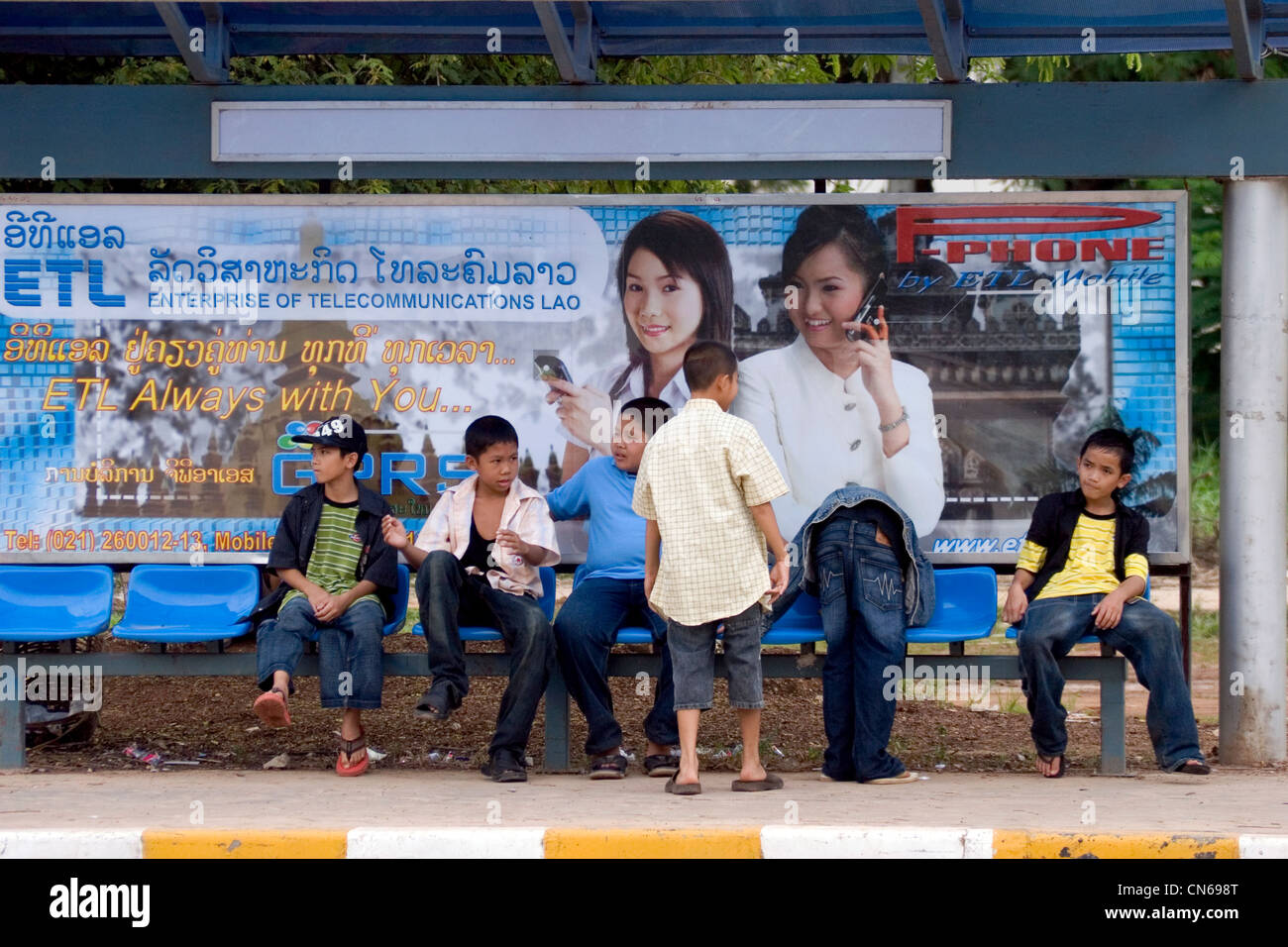 A group of young boys are sitting at a bus stop below a ...