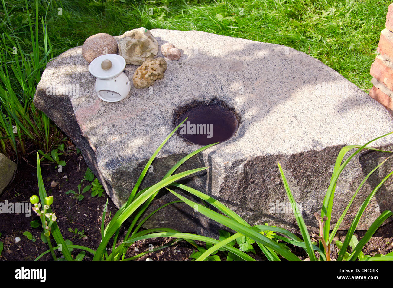 Decorative ancient stone with water in hole and objects on it in garden ...