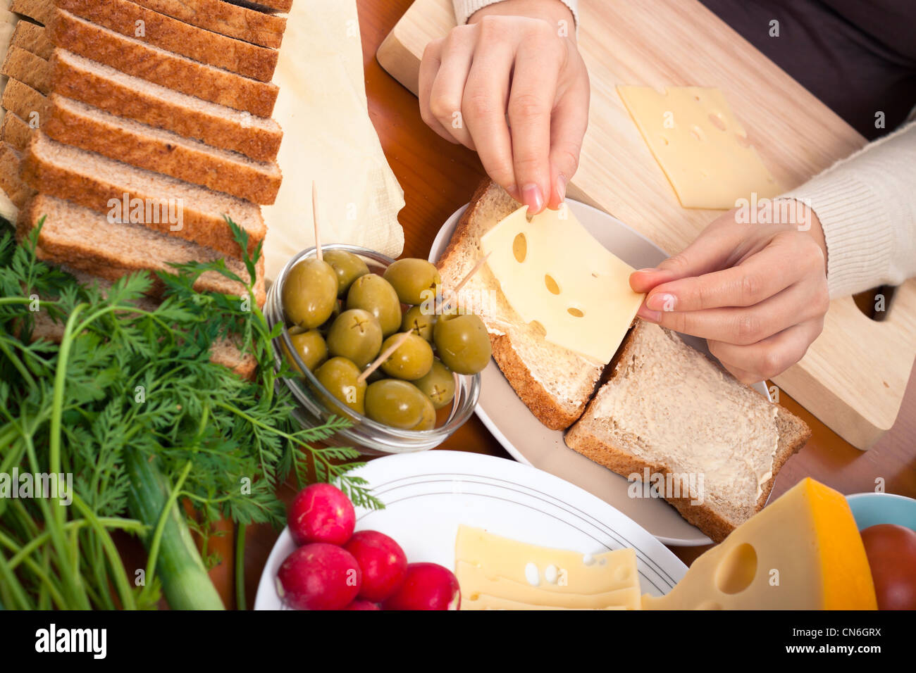 Detail of kitchen table and female hands putting cheese on sandwiches ...