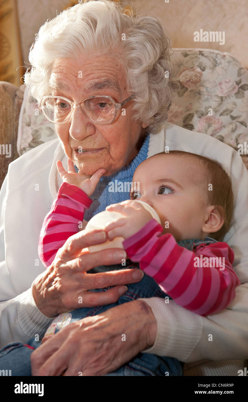 Doting bespectacled grey haired Grandmother, Granny, Nan bottle feeding ...