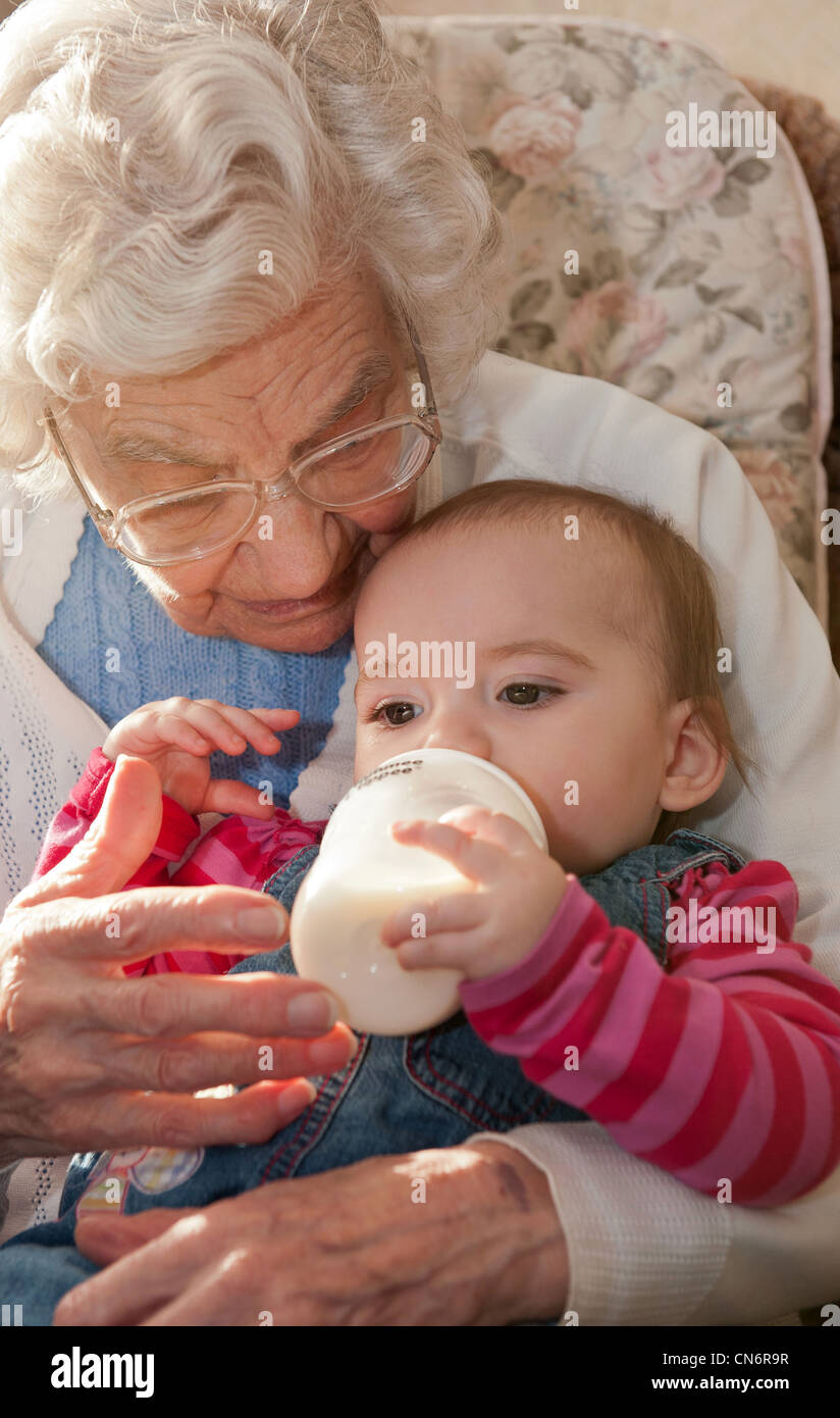 Doting bespectacled grey-haired Grandmother, granny, nan bottle feeding ...