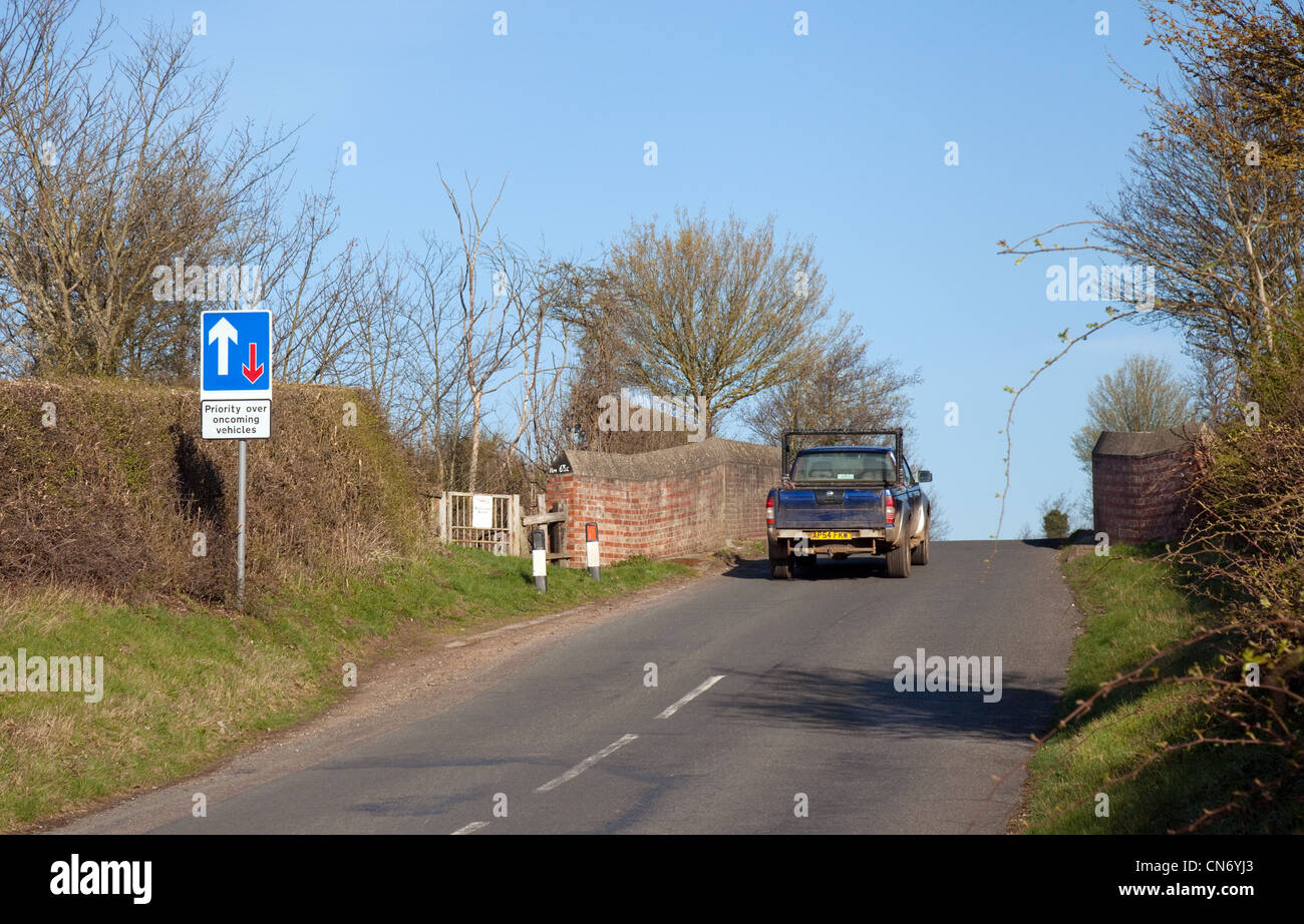 A car going over a humpback bridge on a country road cambridgeshire UK ...