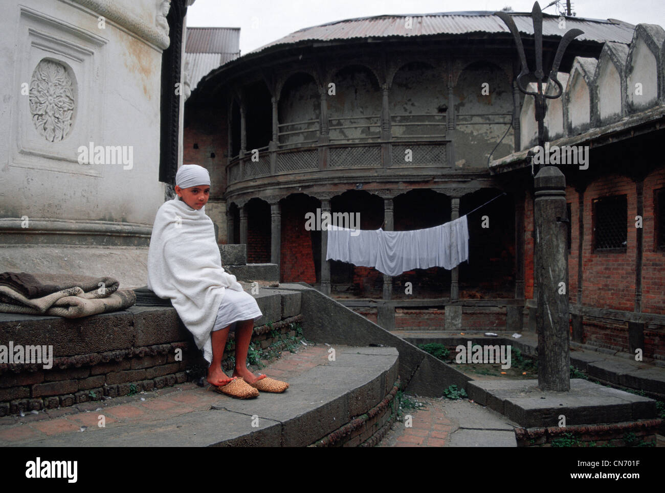 A hindu boy in traditional dress is seated near a temple : he is ...