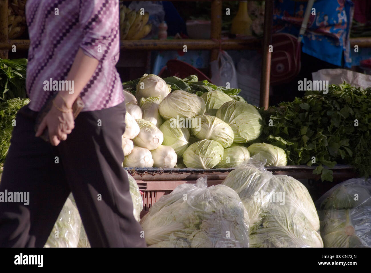A woman is walking past fresh cabbage that is awaiting customers in the ...