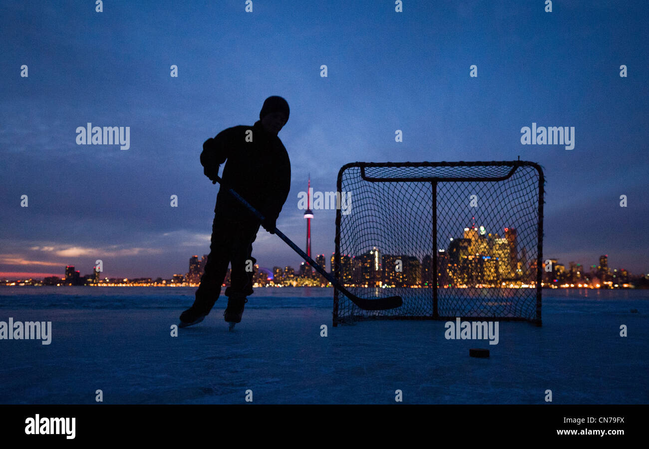 A boy plays hockey on frozen Lake Ontario in front of the skyline of ...